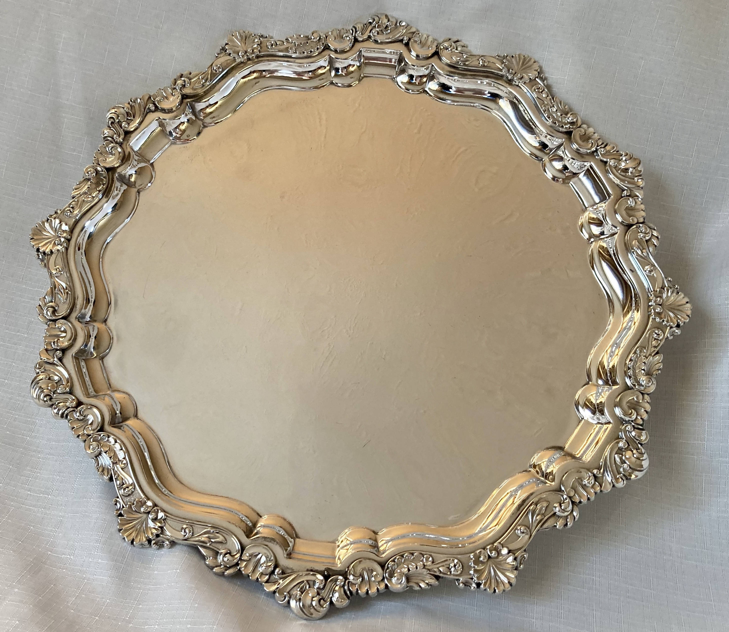 Large silver plated circular salver with shell and scroll border, rais